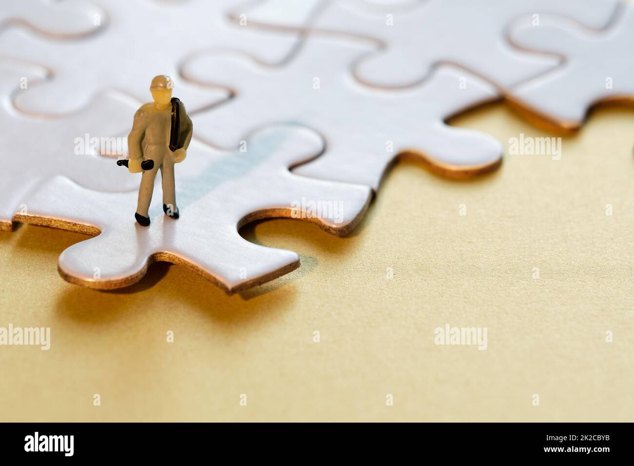 Single tiny worker figure on edge of linked jigsaw puzzle pieces. Close ...