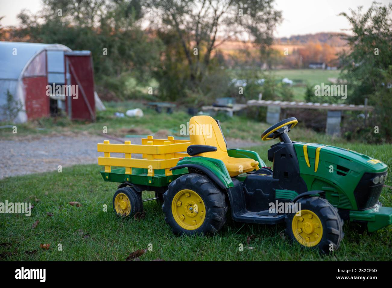 Green and yellow child's toy riding tractor in green grass yard farm ...