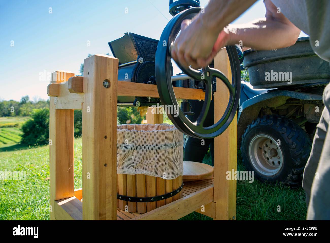 A man turns the flywheel of the apple grinder on a cider press with ATV ...