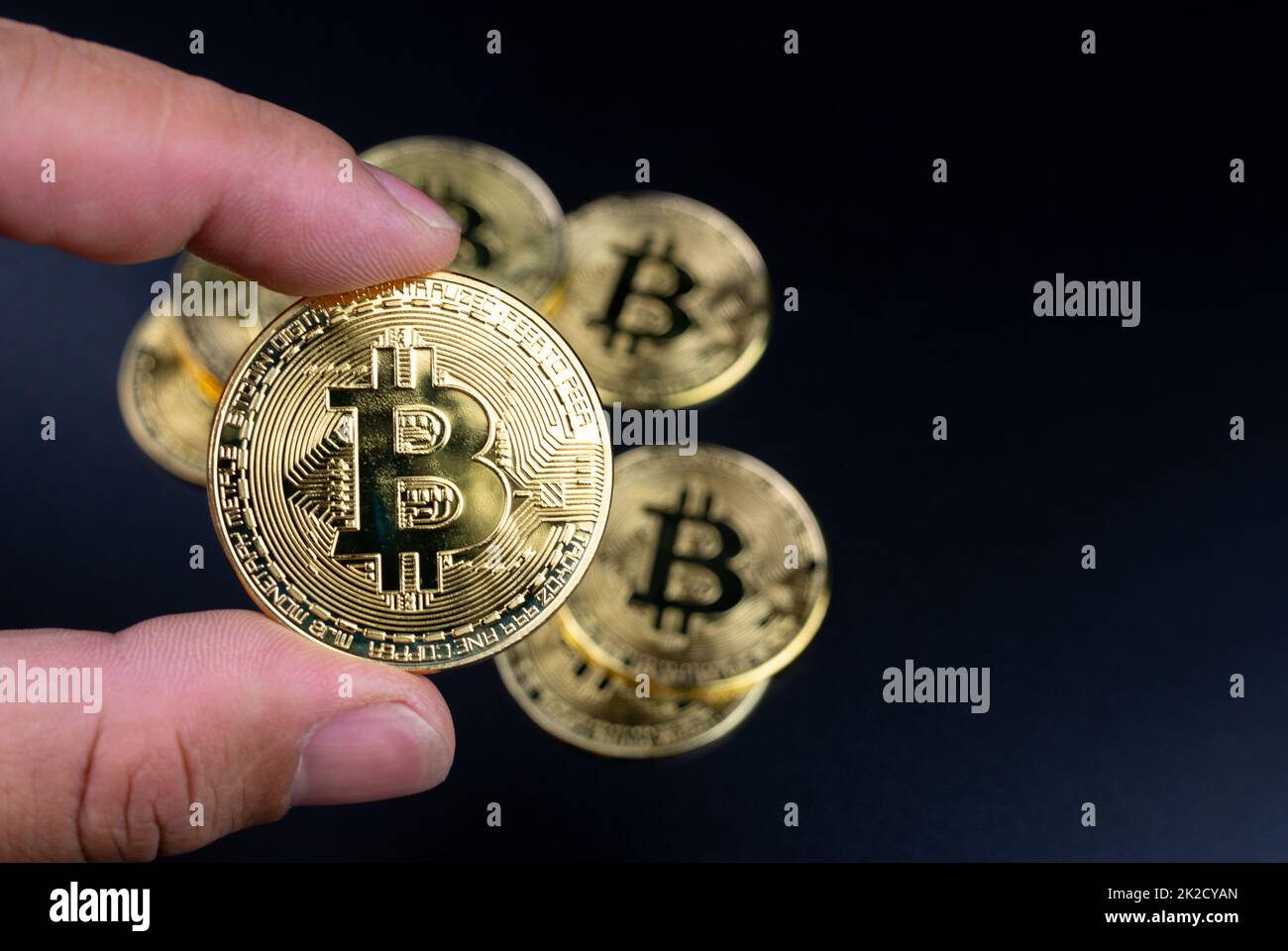 Human fingers holding bitcoins on a black background Stock Photo - Alamy
