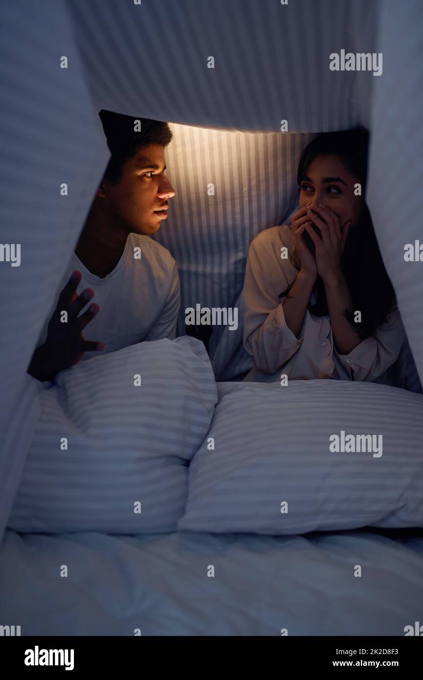 Husband telling wife scary story for under blanket Stock Photo - Alamy