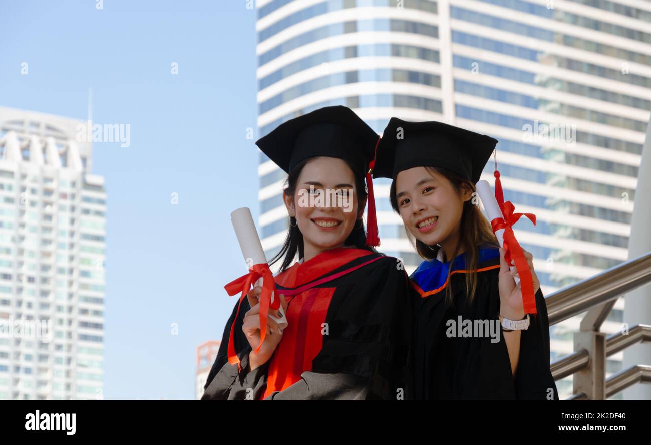 Two graduated women friends holding diplomas in hands and celebrating ...