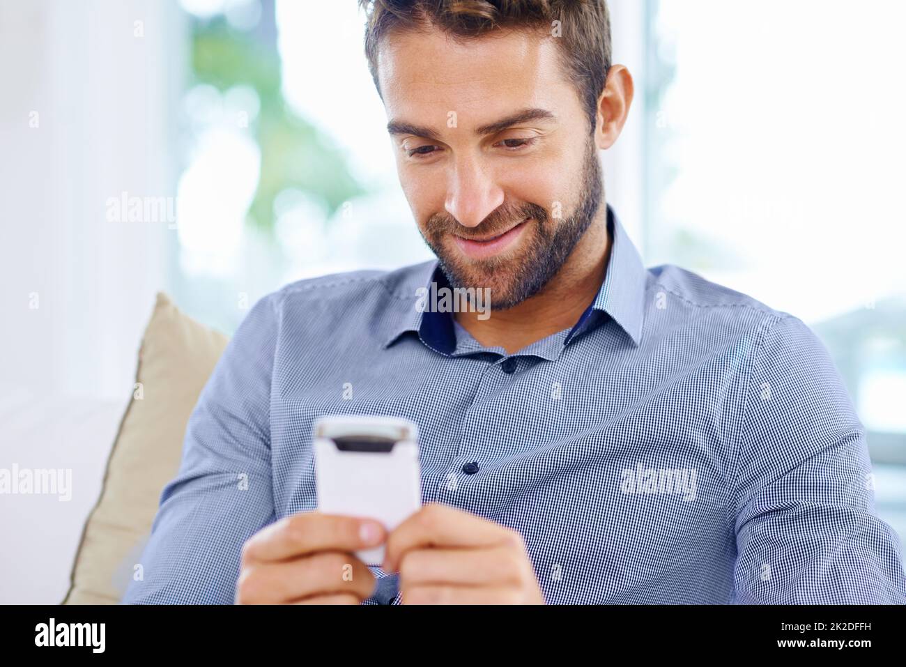 Making the most of his apps. Man using his cell phone in his lounge ...