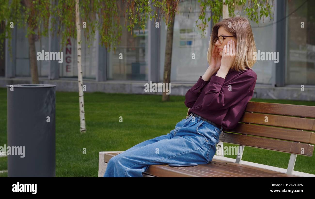 Woman suffering bad headache touching her temples outside sitting on a ...