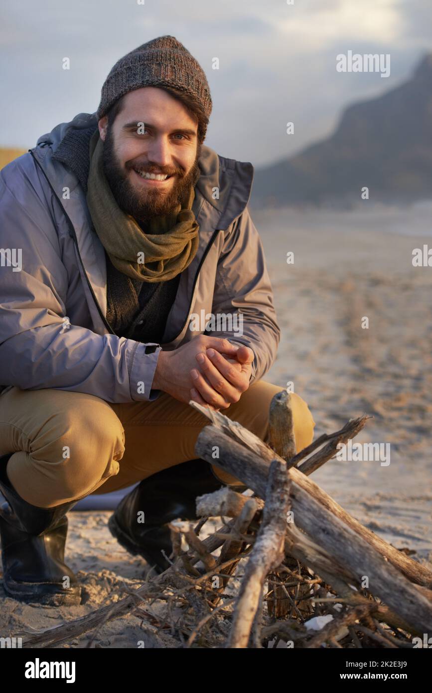 Itll get warm soon. A young man building a fire on the beach Stock ...