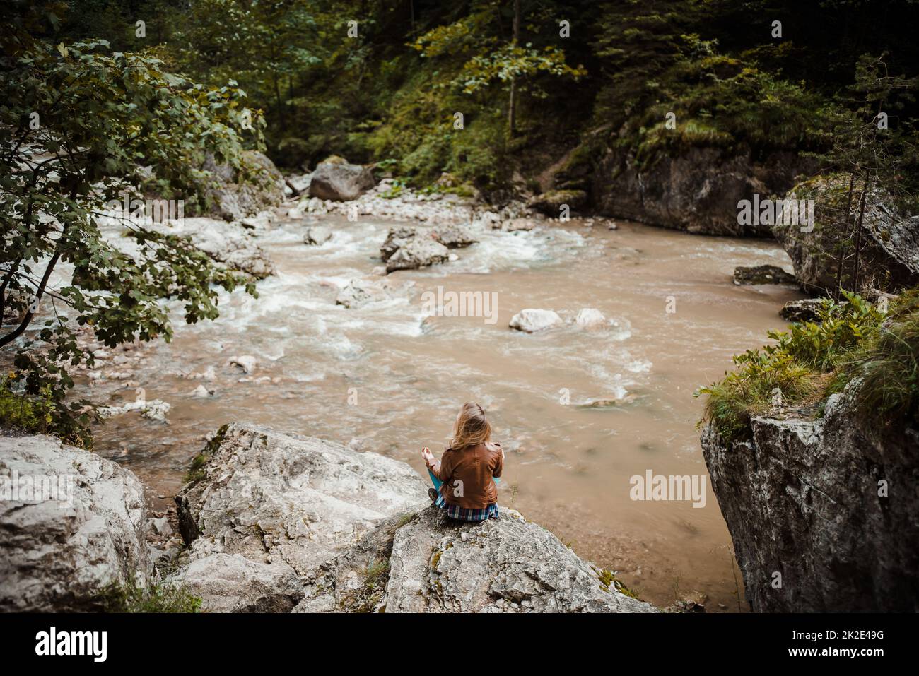 Young woman standing on the edge of a waterfall and practicing yoga ...