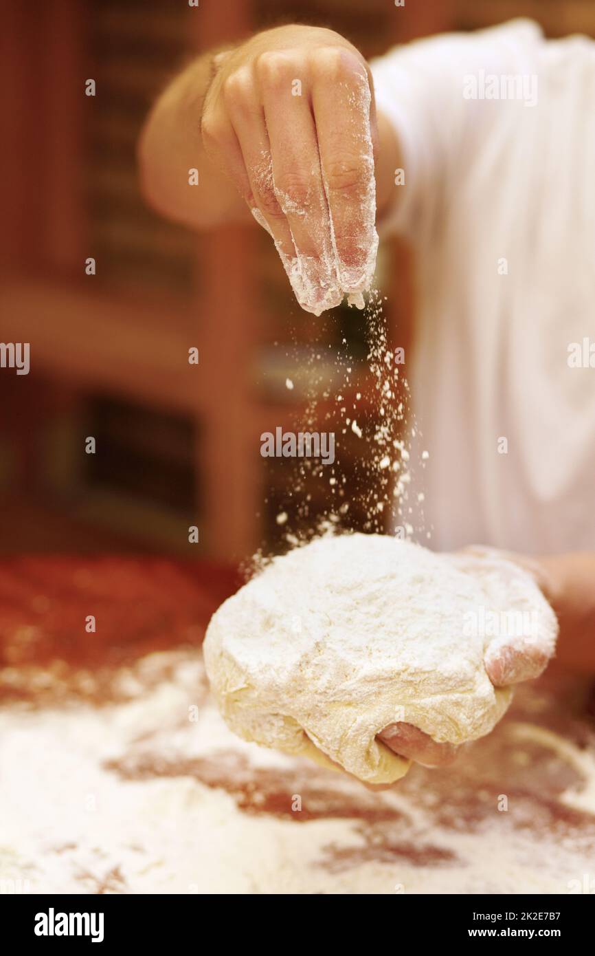 Making sure it wont stick. Hands sprinkling flour on a ball of dough ...