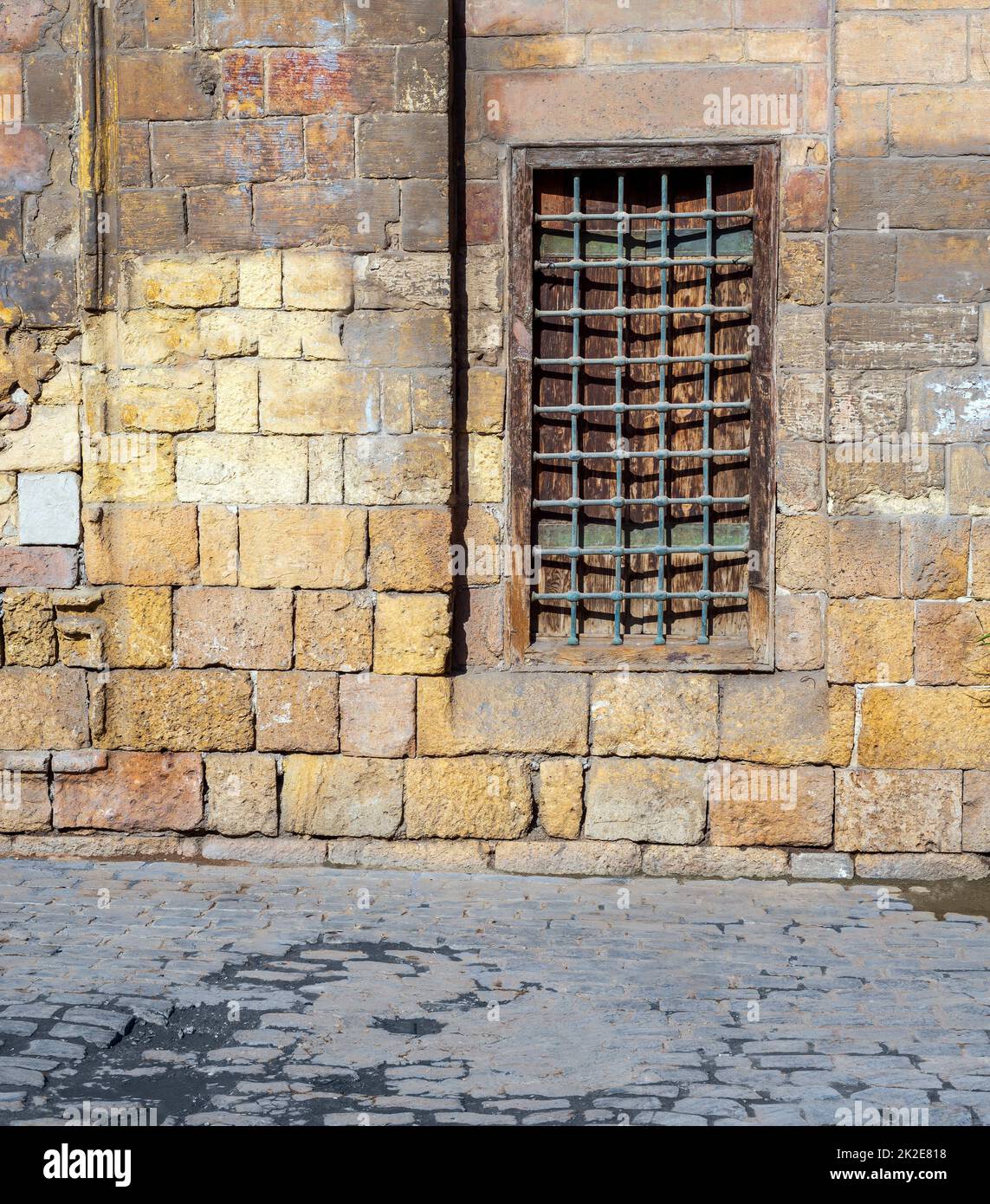 Grunge wooden window with decorated iron grid over stone bricks wall ...