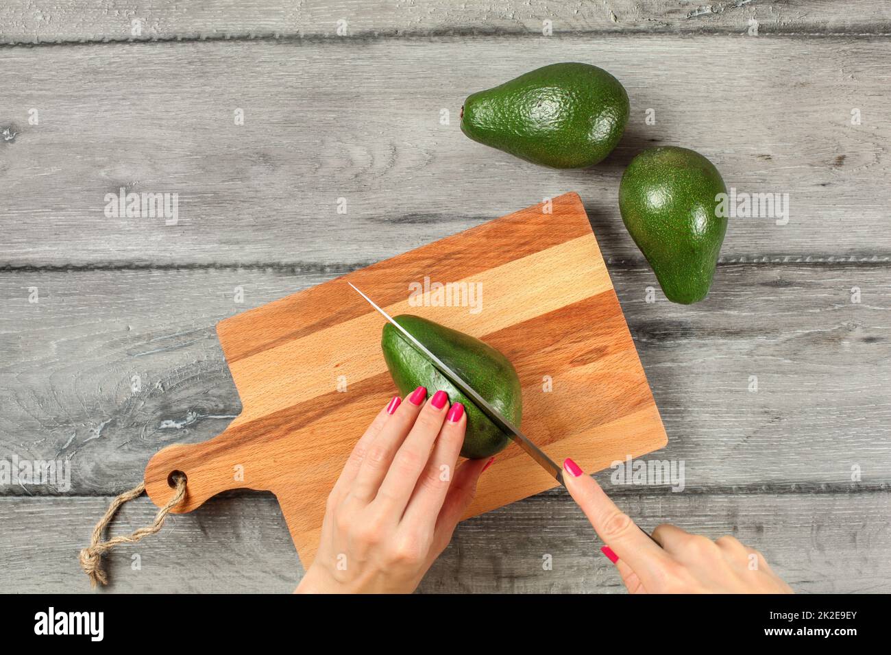 Tabletop view, young woman cutting whole avocado on chopping board ...