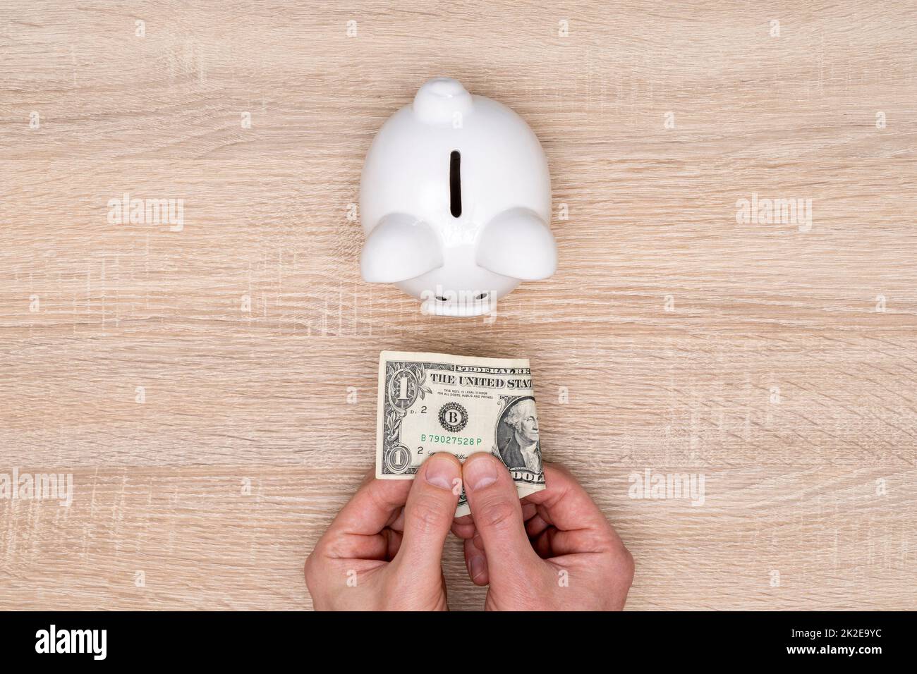 Hands holding one dollar opposite of piggy bank Stock Photo - Alamy