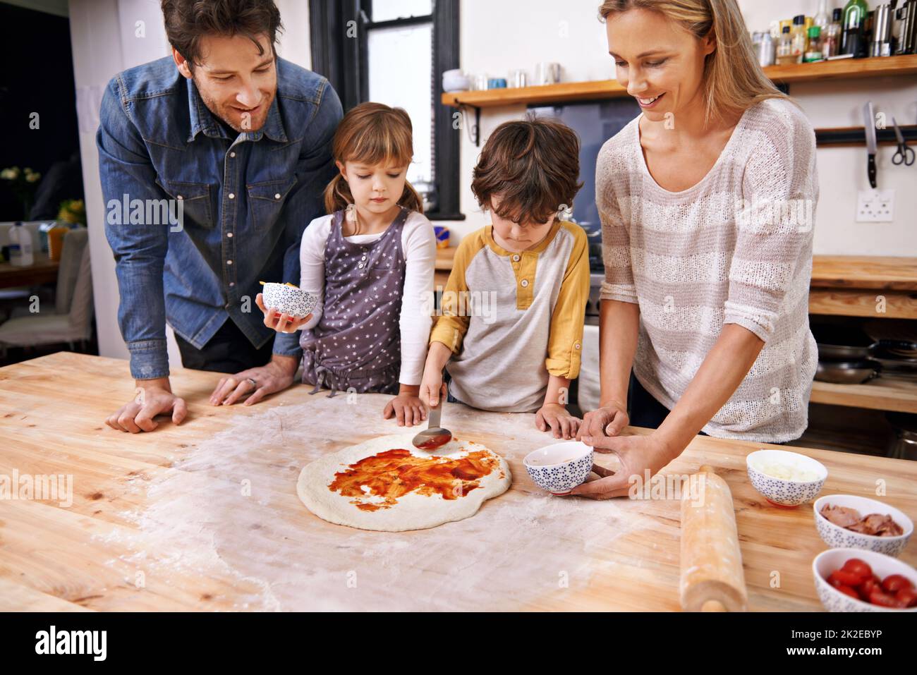 Adding the tomato base...A family making pizza together at home Stock ...