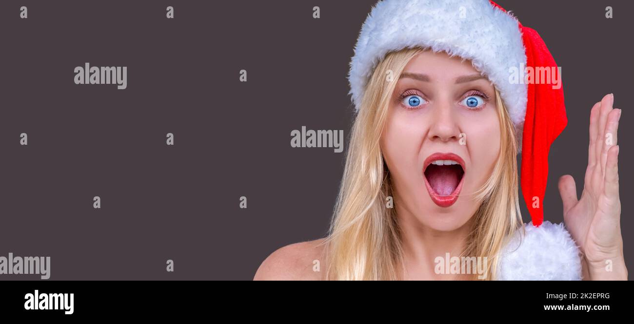 Portrait of surprised woman with her mouth open in a santa hat staring ...