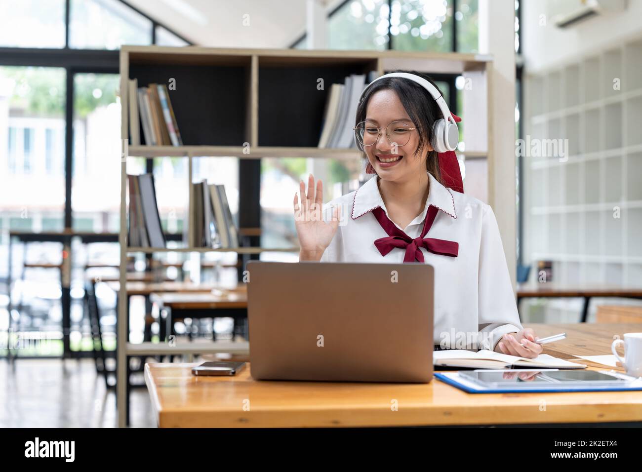 Smiling asian woman in headset waving hand, using laptop, looking at ...