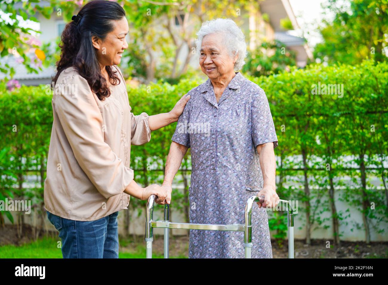 Caregiver help Asian elderly woman disability patient walk with walker in park, medical concept ...