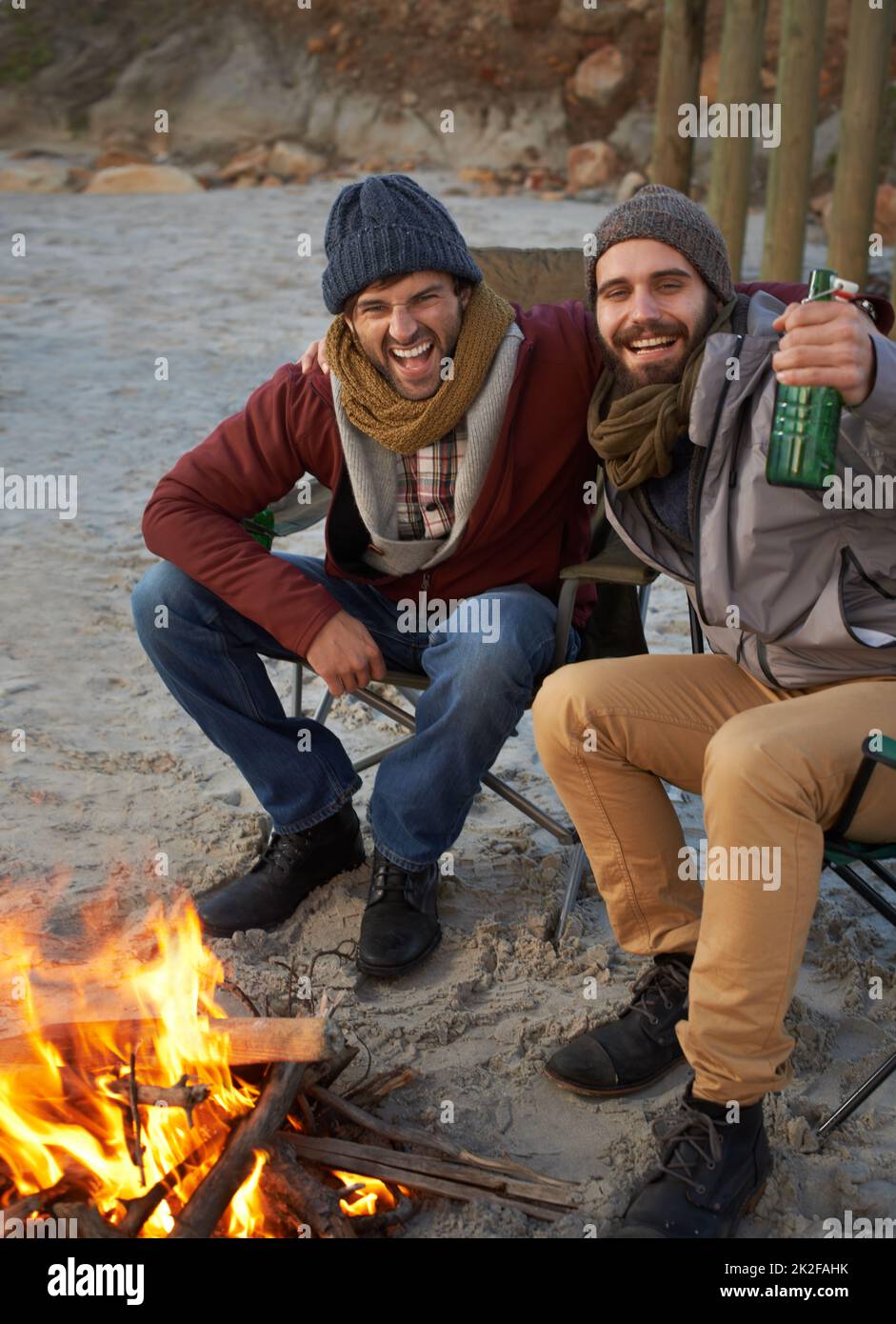 Warming up with a fire and a beer. Two young men sitting around a fire ... Warming up with a fire and a beer. Two young men sitting around a fire ...
