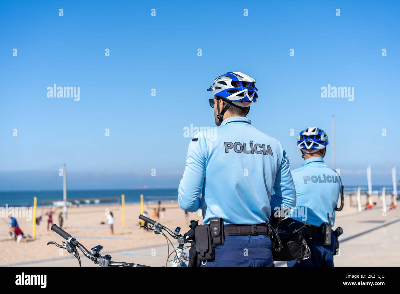 Two policeman patrolling seaside promenade on bicycles. People are ...
