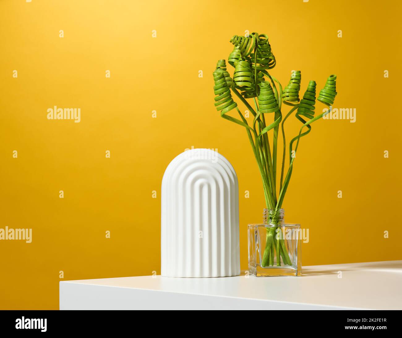 transparent vase with green plants and a white arch on a yellow ...