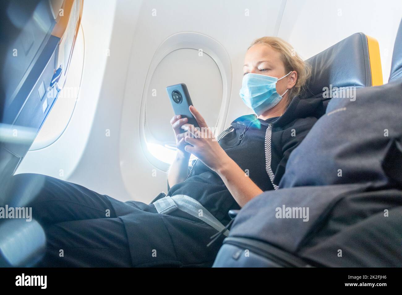 A young woman wearing face mask, using smart phone while traveling on ...