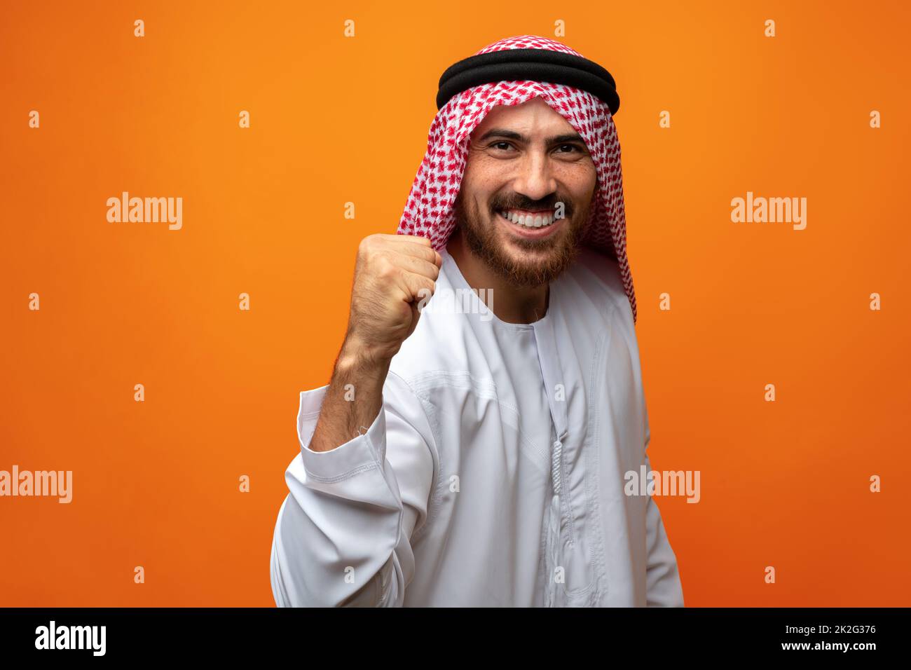 Successful smiling young Arab man celebrating victory on orange ...