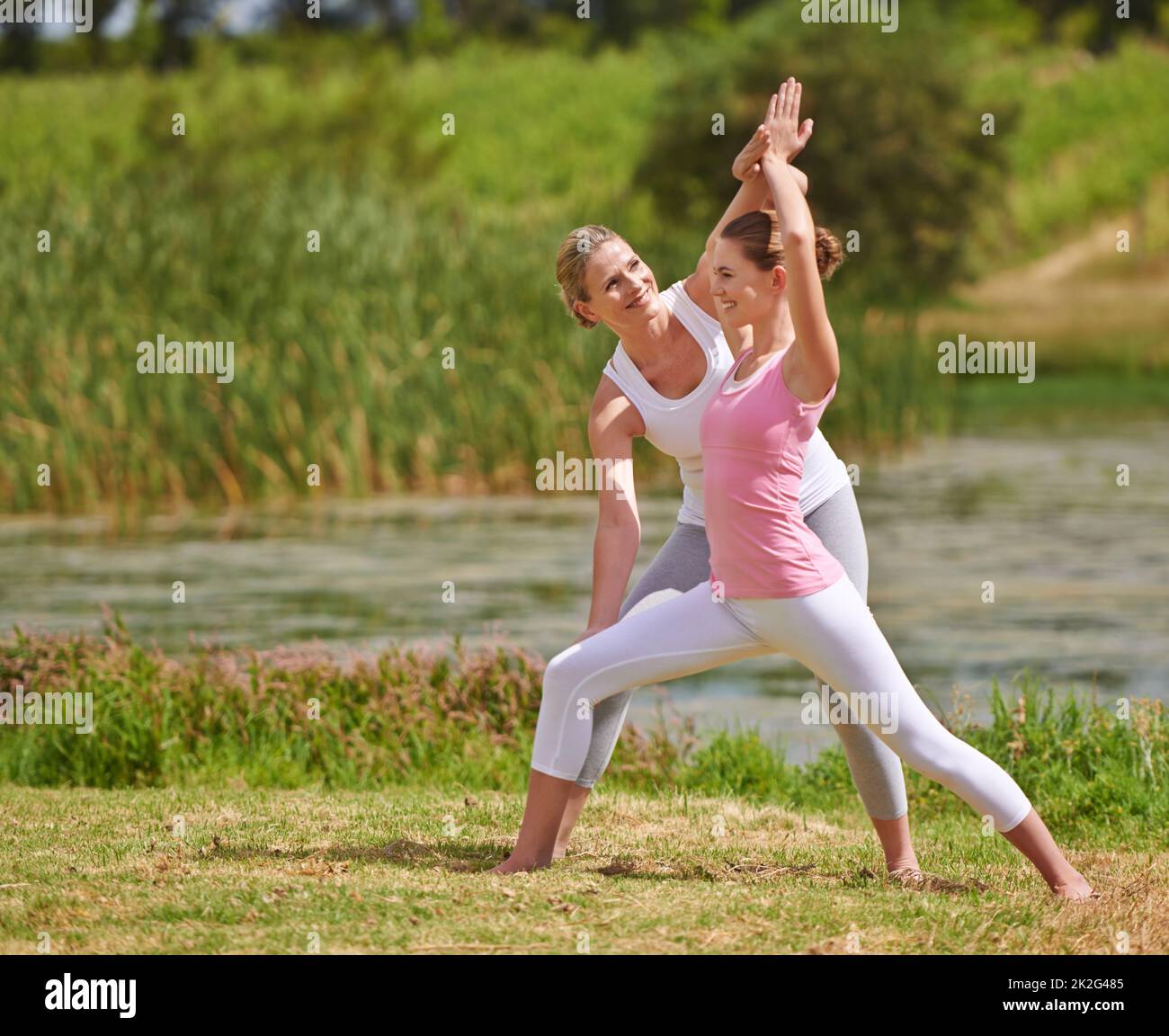 Feeling the stretch. a young woman being instructed in an outdoor yoga ...