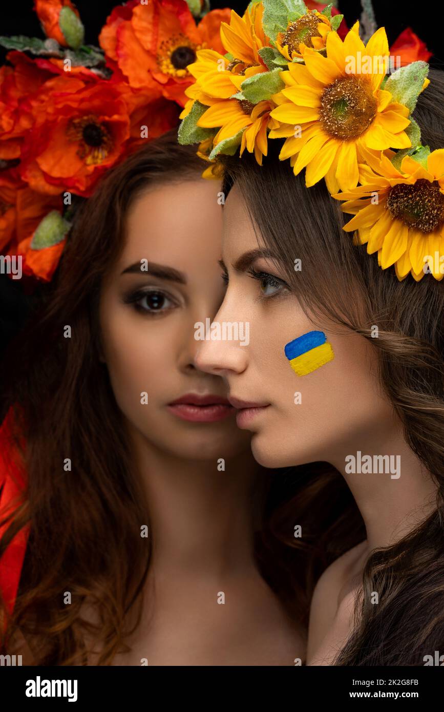 Two beautiful girls in flower wreaths of red poppy and yellow sunflower ...