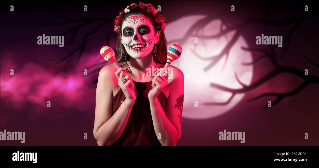 Young woman with painted skull on her face and maracas at night ...