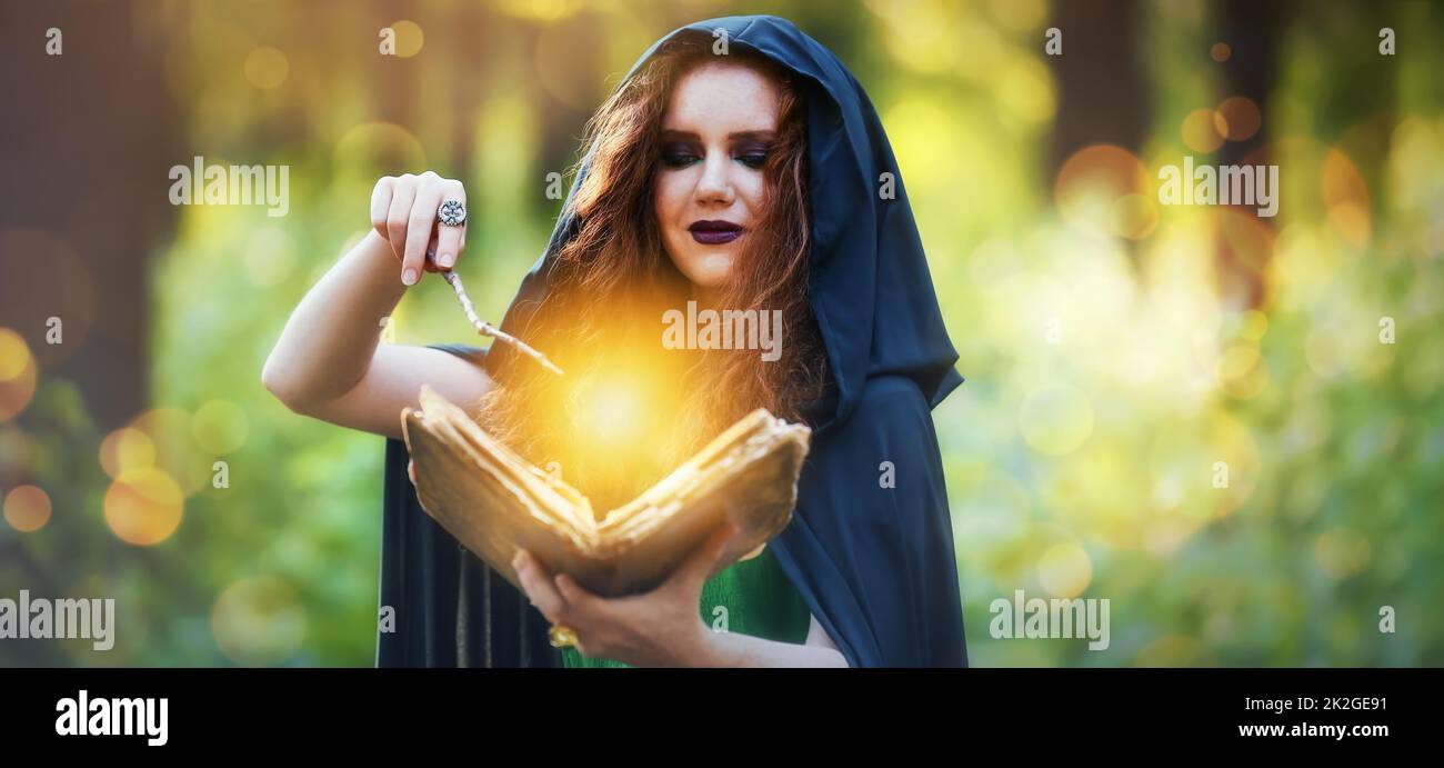 Young witch with spell book and magic wand in green forest Stock Photo ...