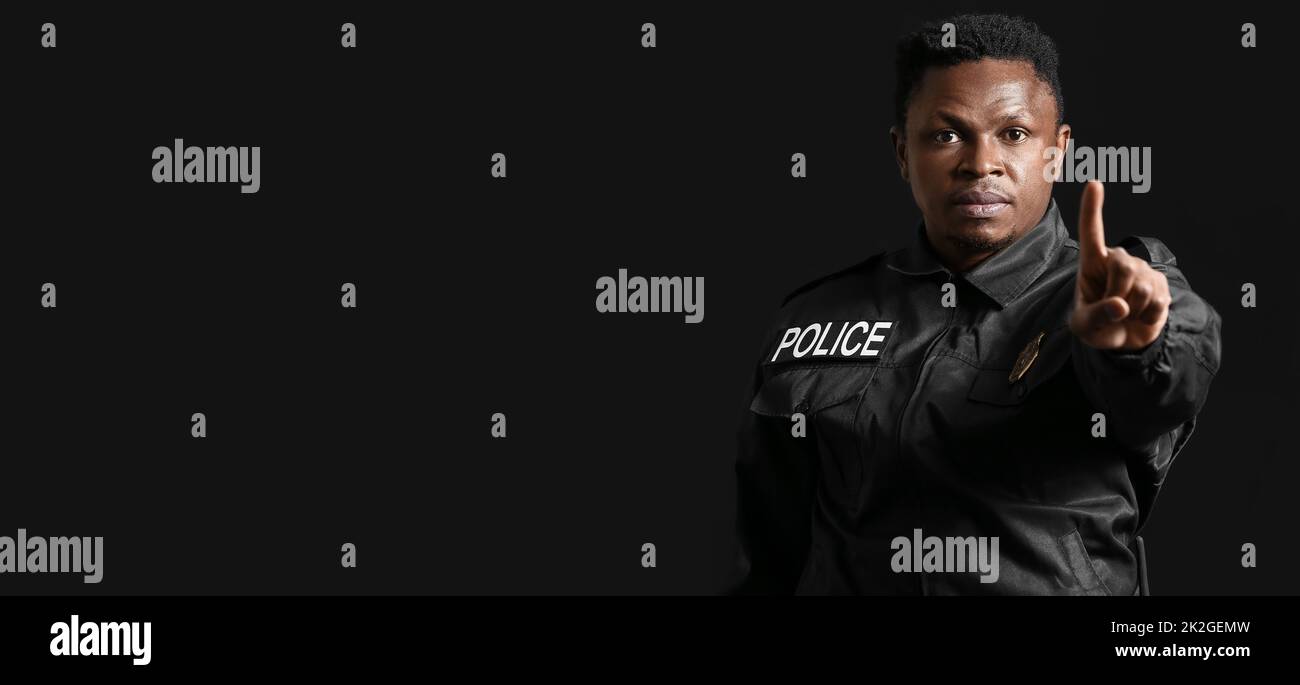 African-American police officer pointing at viewer on dark background ...