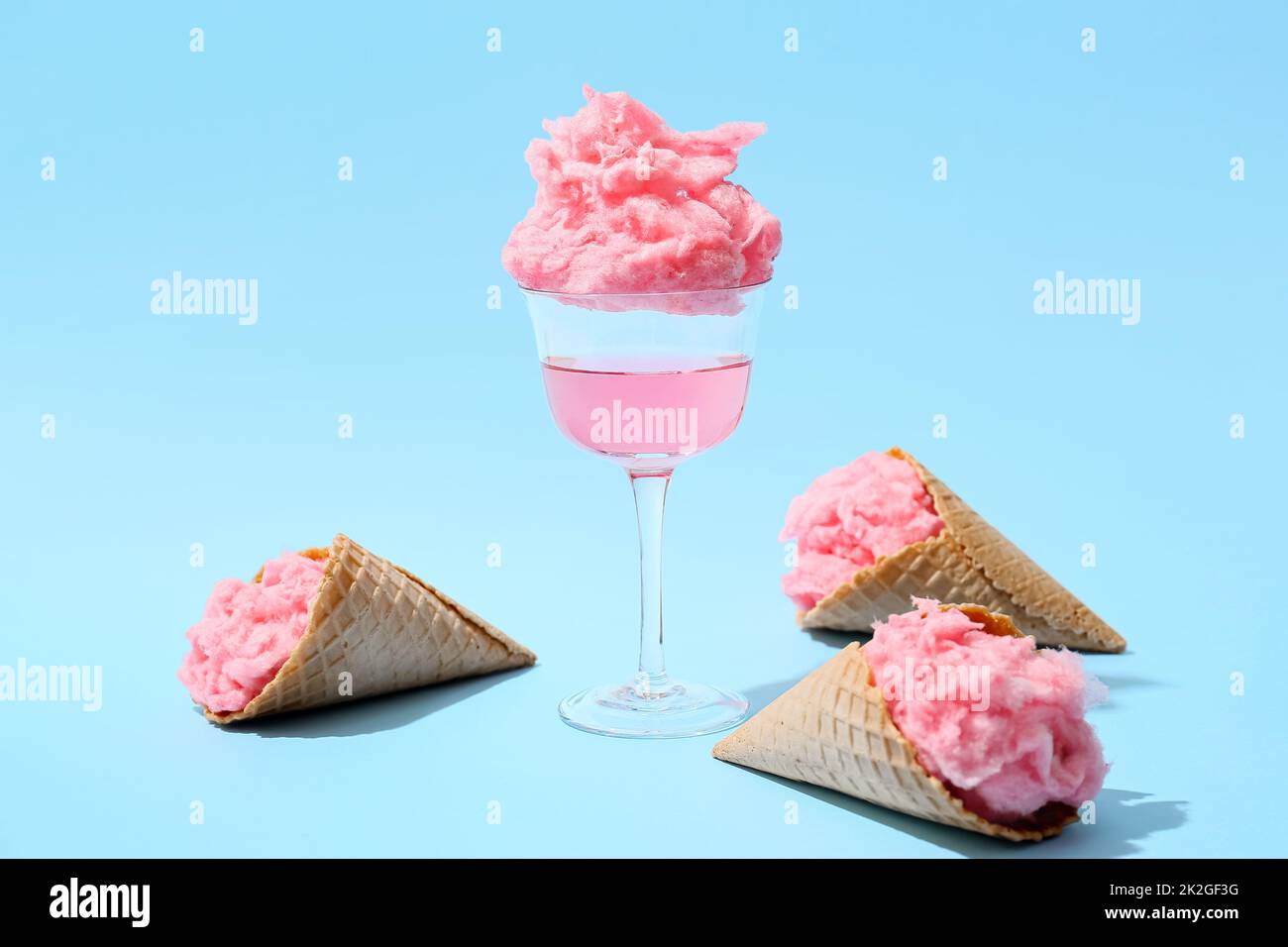 Glass with tasty cotton candy cocktail and waffle cones on color ...