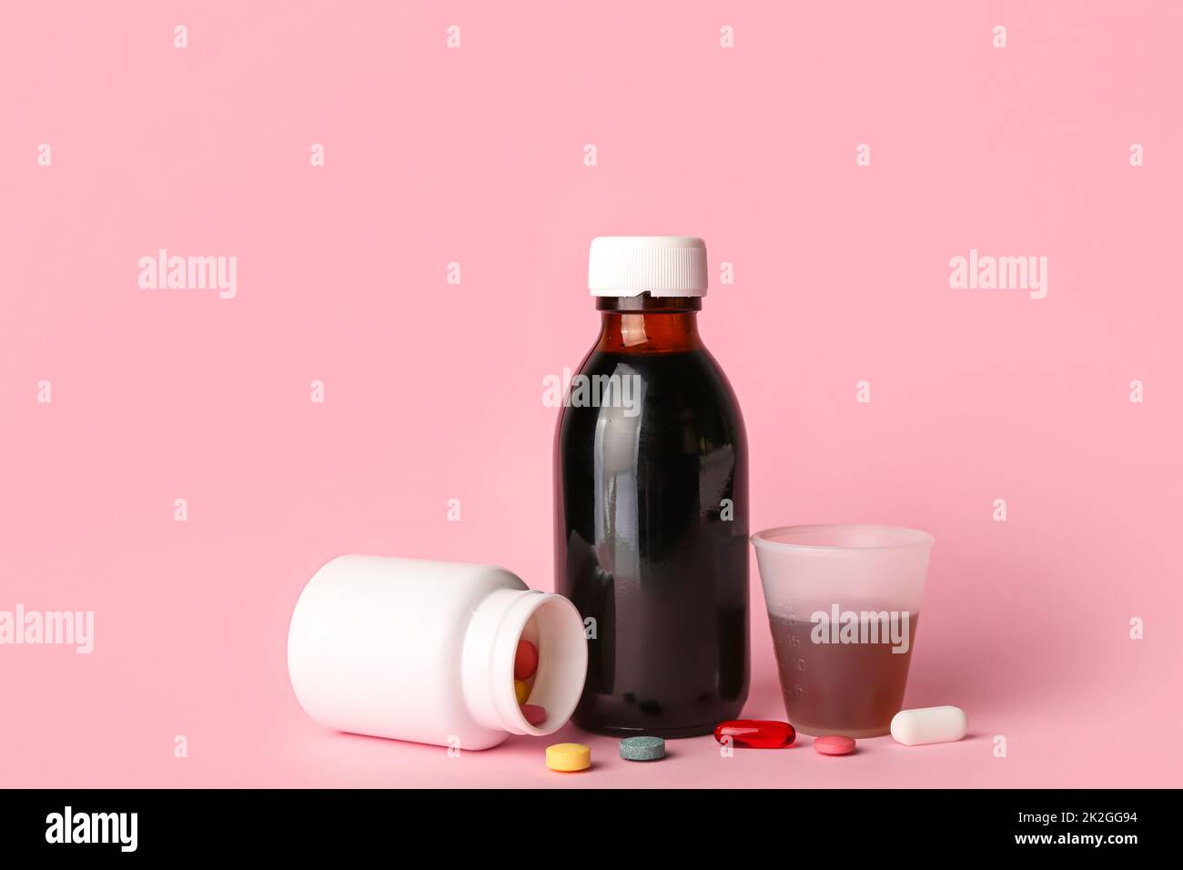 Bottle of cough syrup, pills and cup on pink background Stock Photo - Alamy