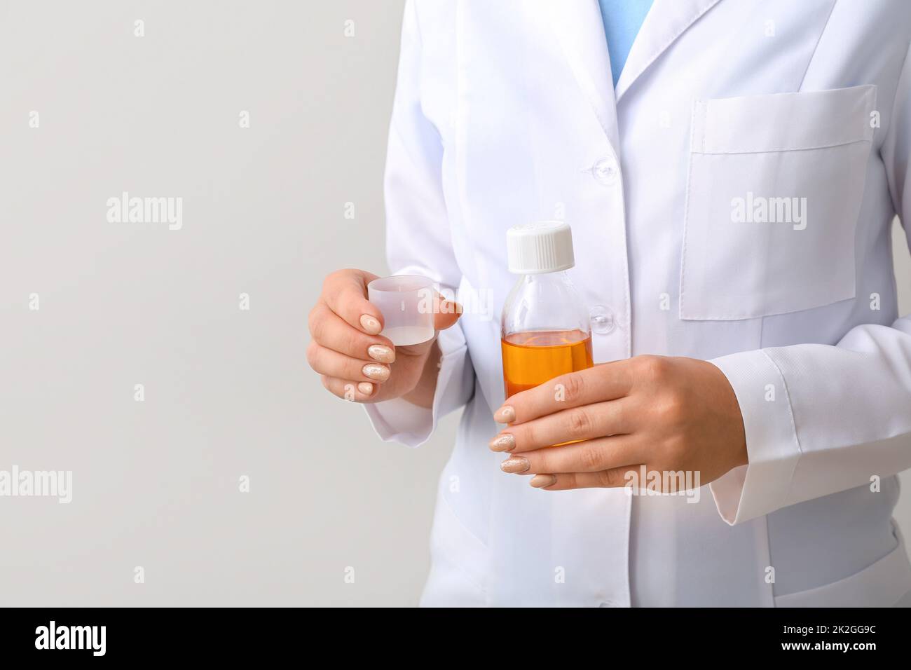 Female doctor with bottle of cough syrup and cup on grey background ...