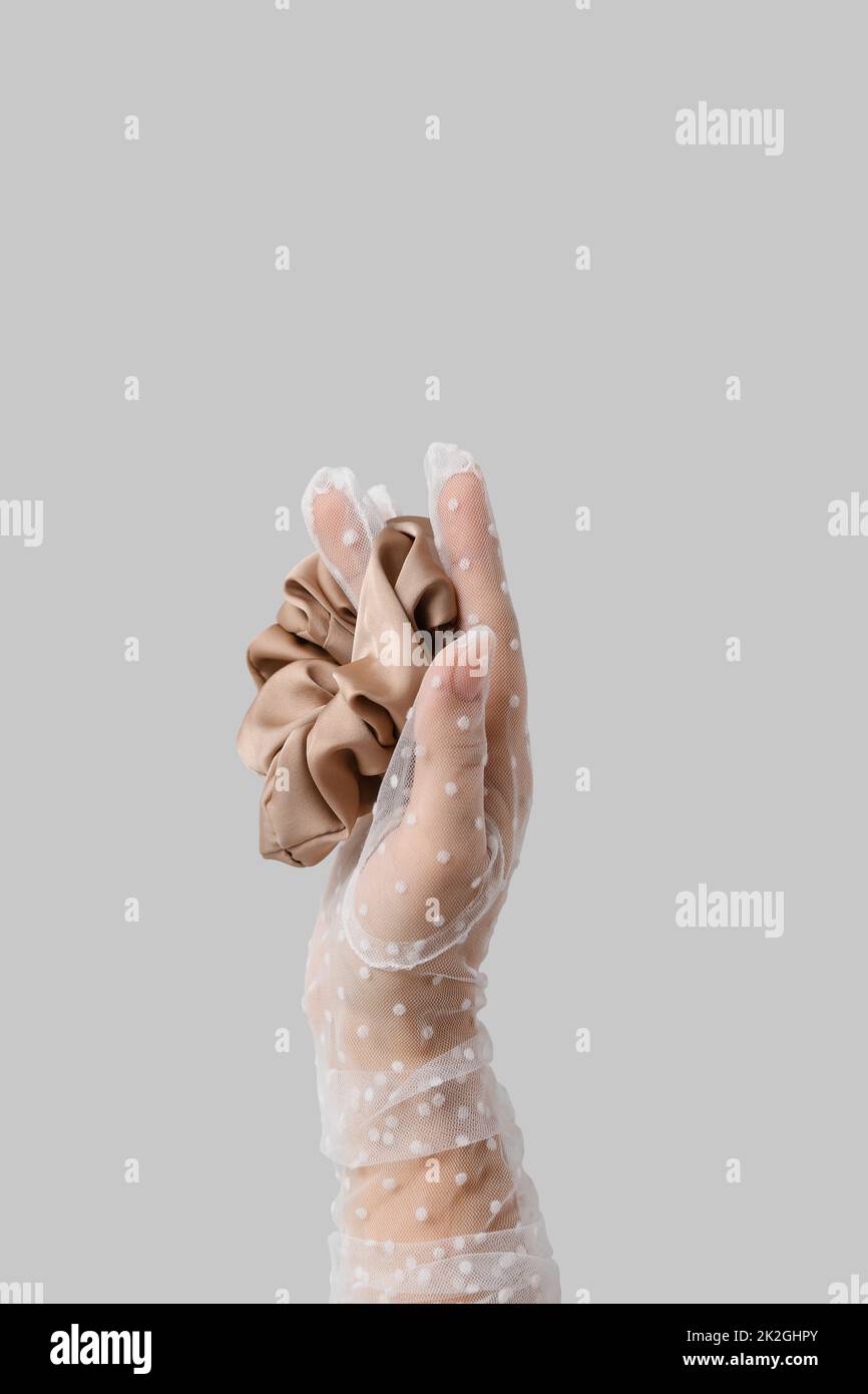 Female hand in glove with silk scrunchy on light background Stock Photo ...