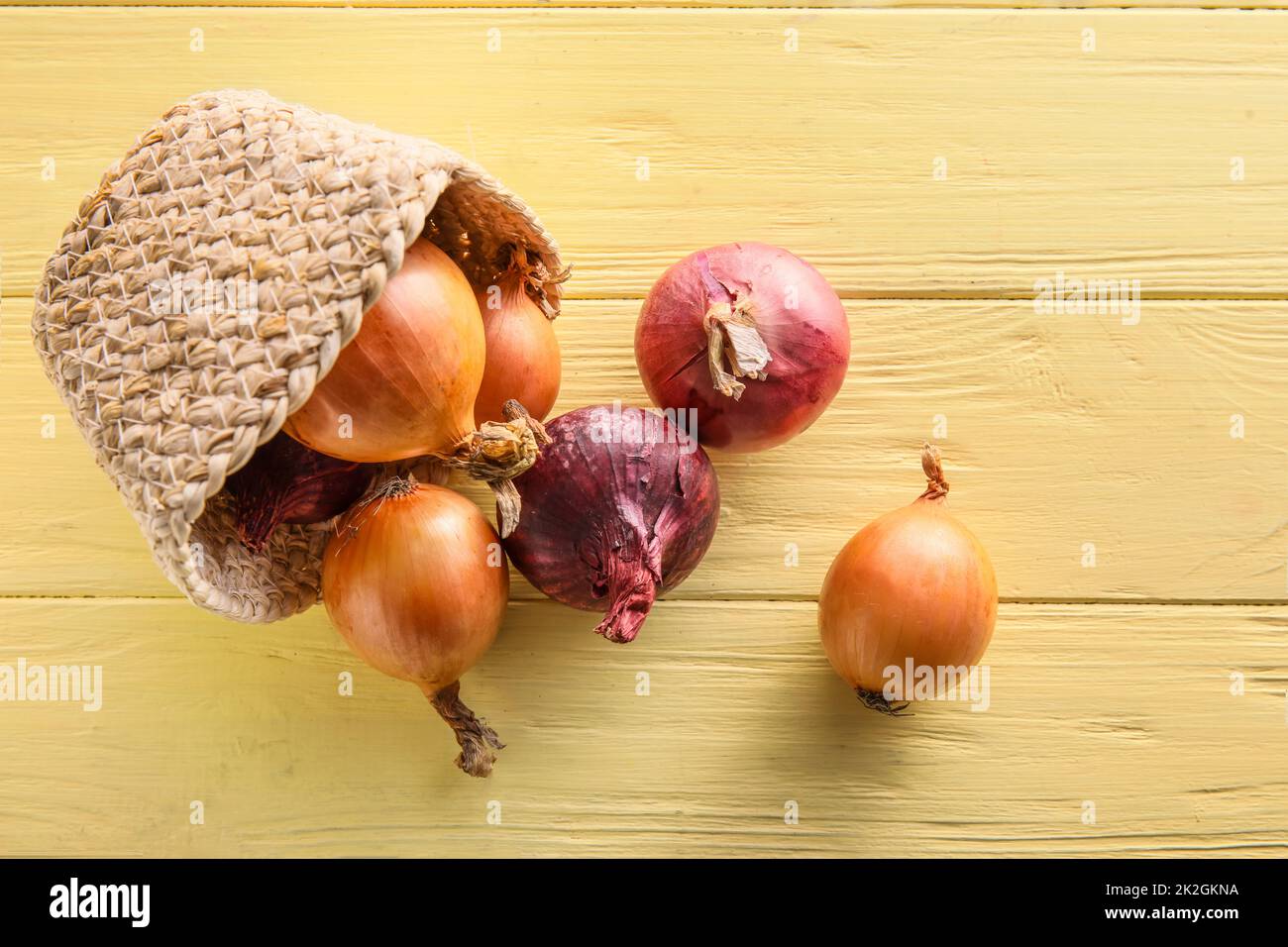 Overturned basket with fresh onion on color wooden background Stock ...