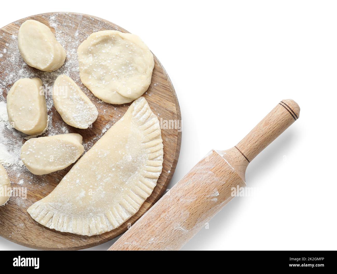 Board with raw cheburek, pieces of dough and rolling pin on white ...