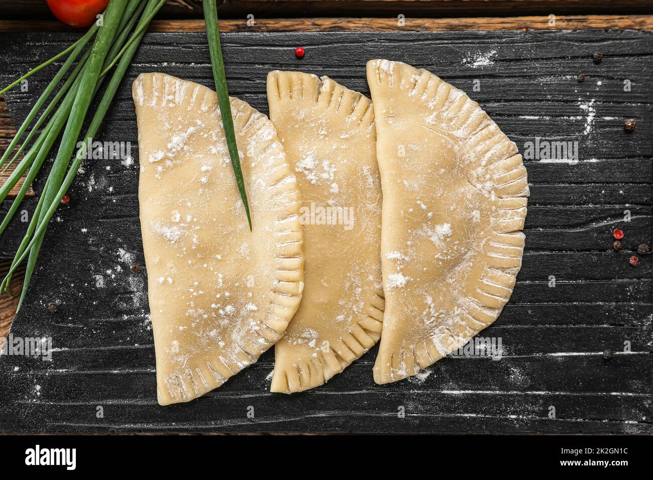 Board with raw chebureks and green onion on wooden background Stock ...