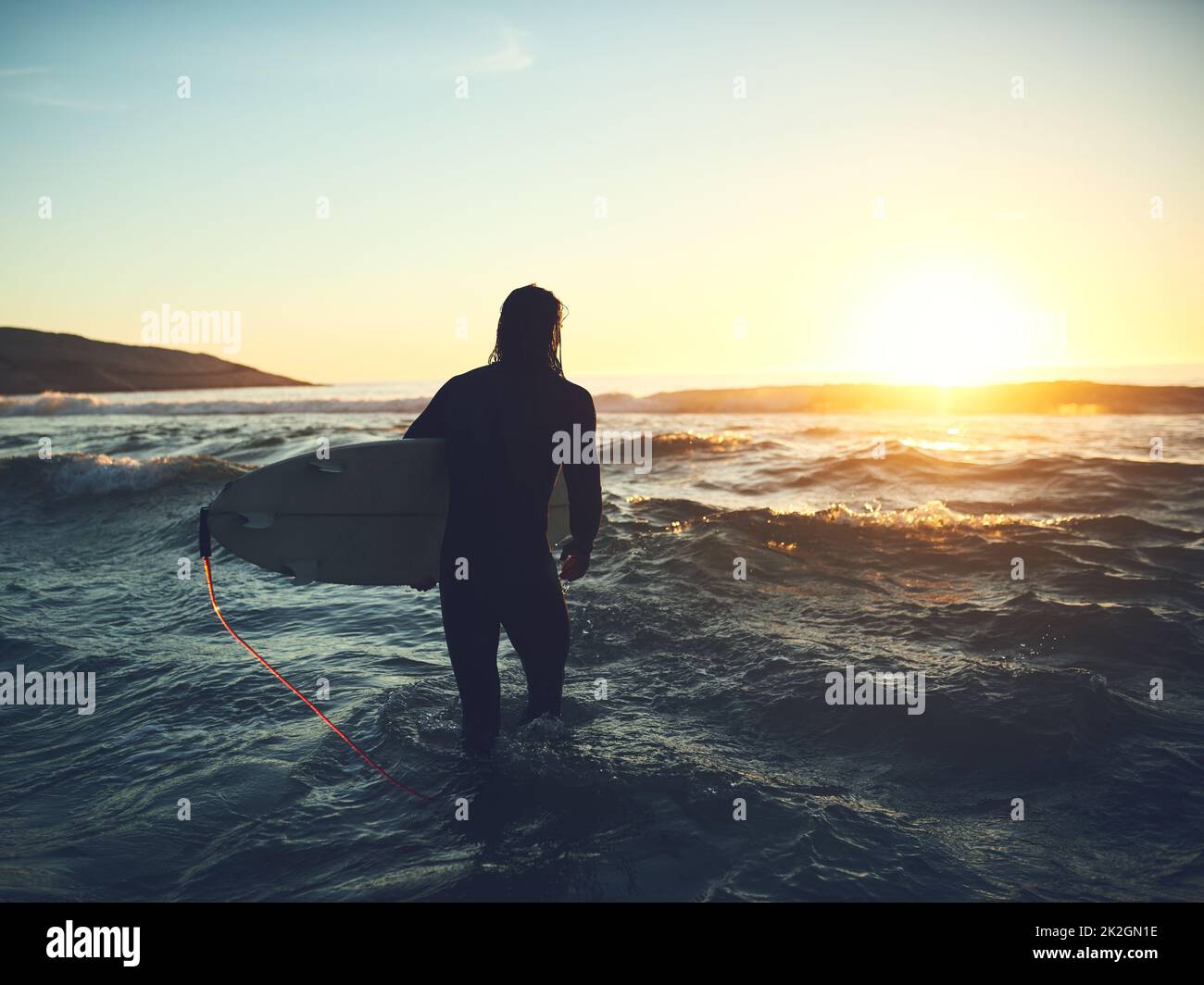 This is home for me. Rearview shot of a young man carrying a surfboard ...
