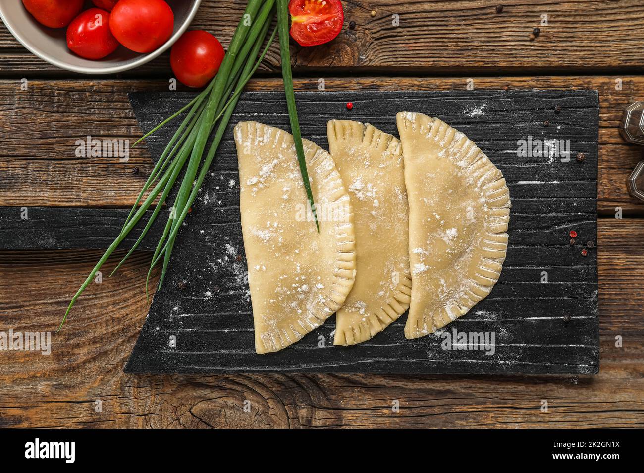 Board with raw chebureks, green onion and tomatoes on wooden background ...