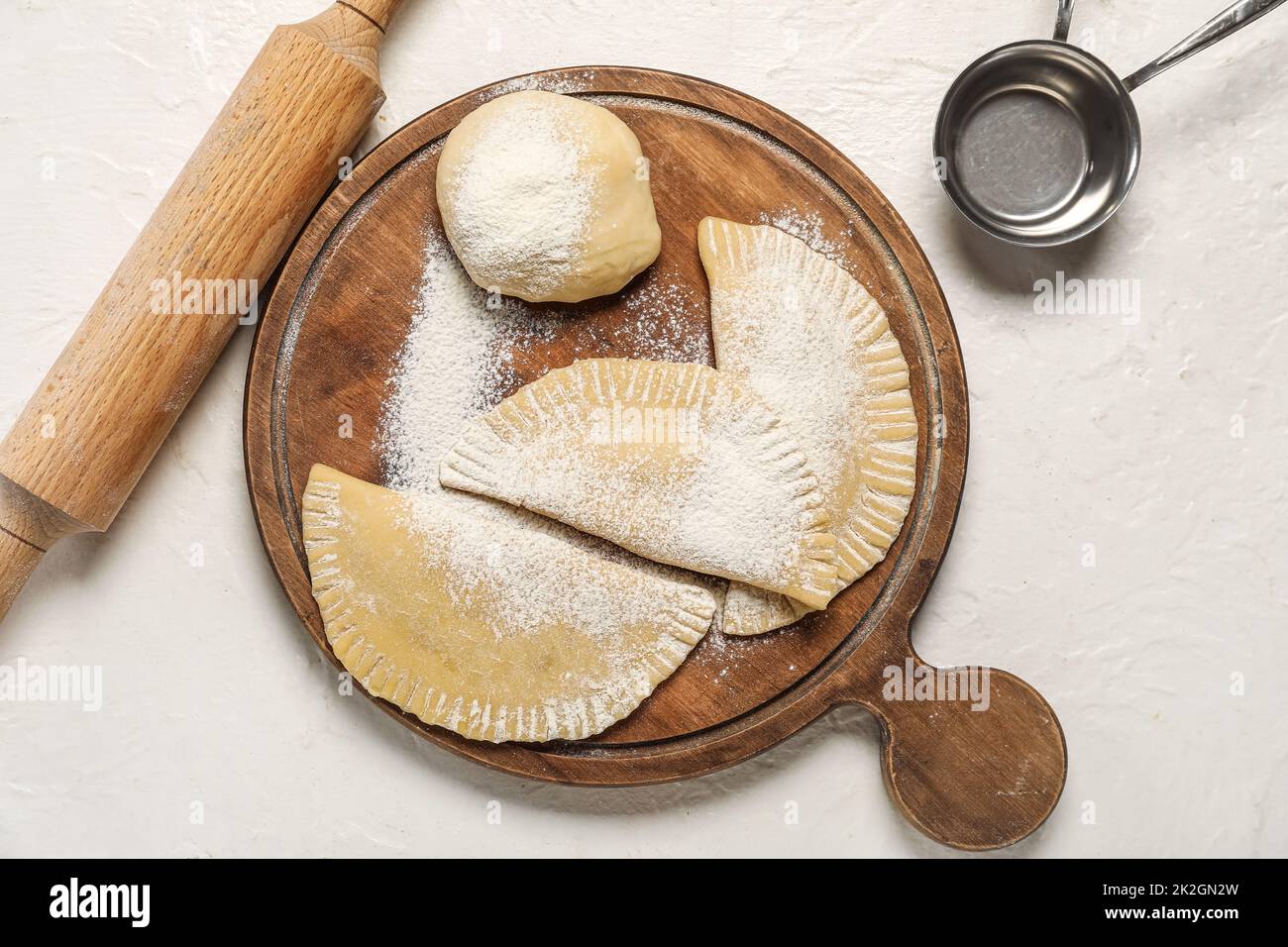 Board with raw chebureks, dough and rolling pin on white background ...