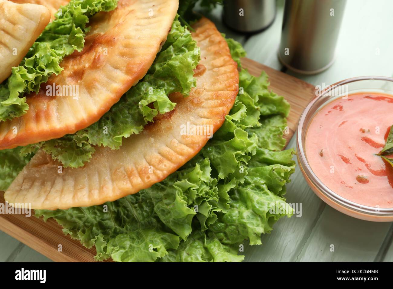 Board with tasty chebureks and lettuce on color wooden background ...