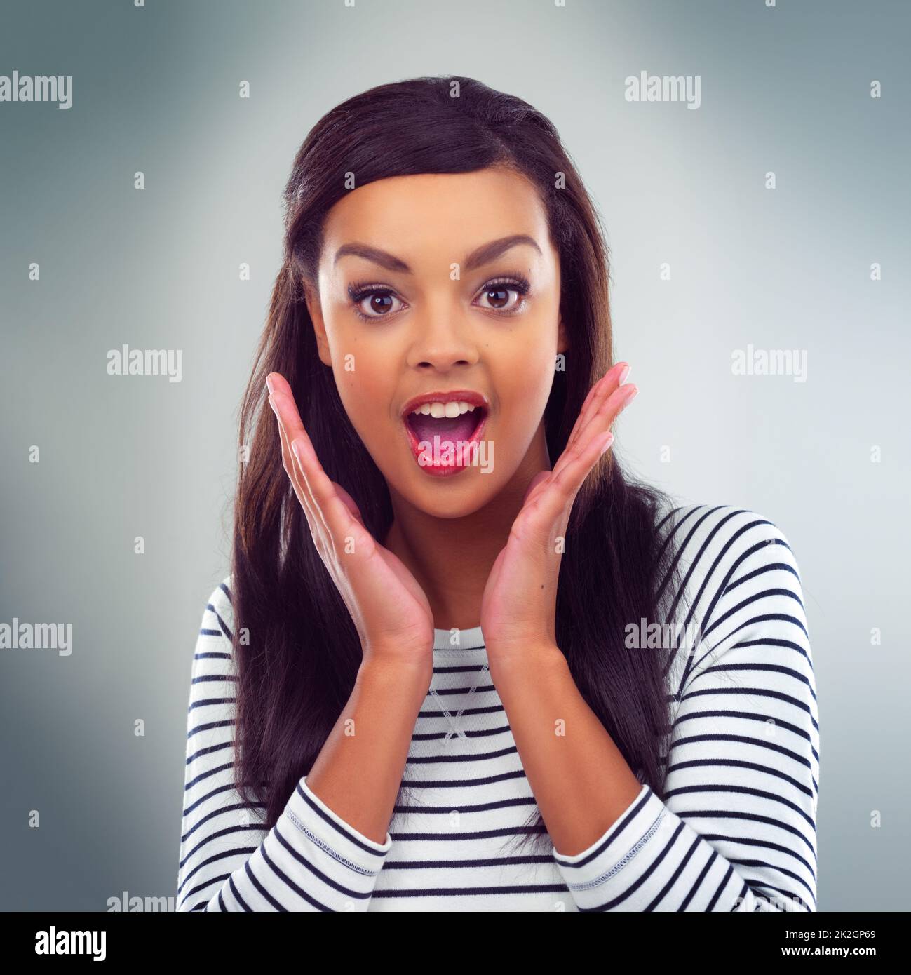 Wow what a pleasant surprise. Shot of a young woman posing against a grey background Stock Photo ...