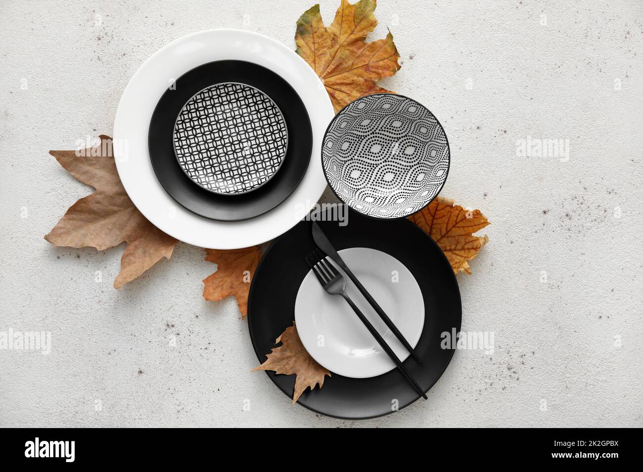 Beautiful plates with cutlery and autumn leaves on white background ...