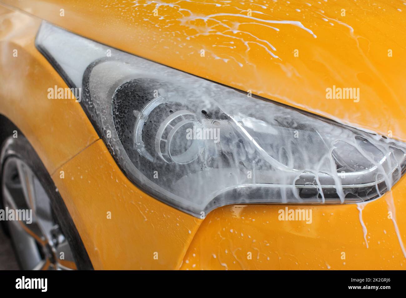 Front light of yellow car washed in carwash, jet water spraying, white ...