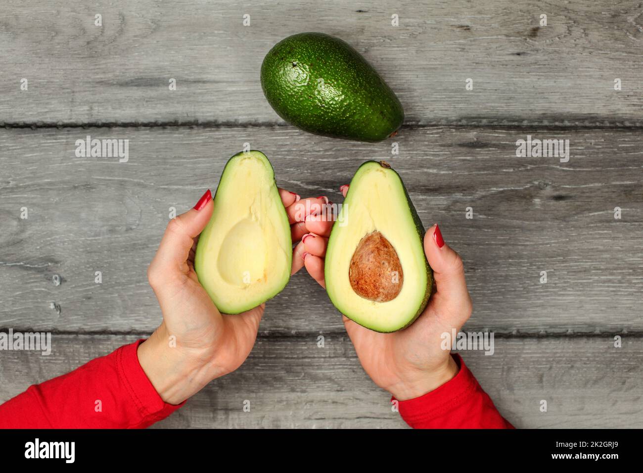 Tabletop view woman's hand holding two avocado halves, seed visible ...