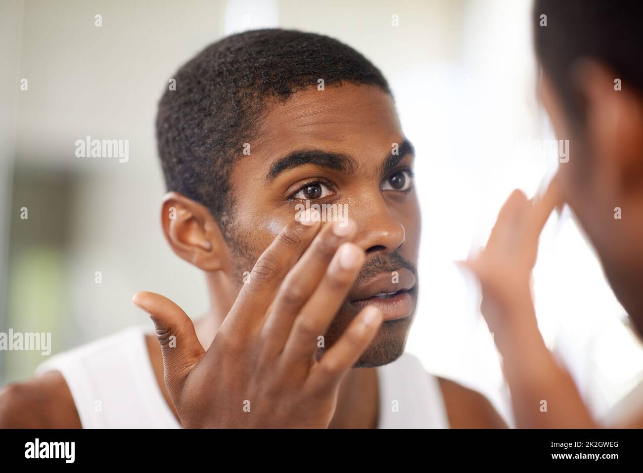He takes care of his skin. A young man applying cream to his face while ...