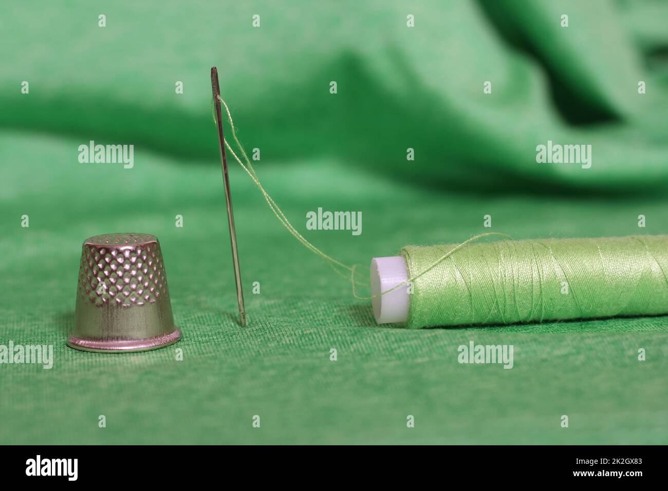Spool of Green Thread, Thimble and Needle on Green Fabric Stock Photo ...