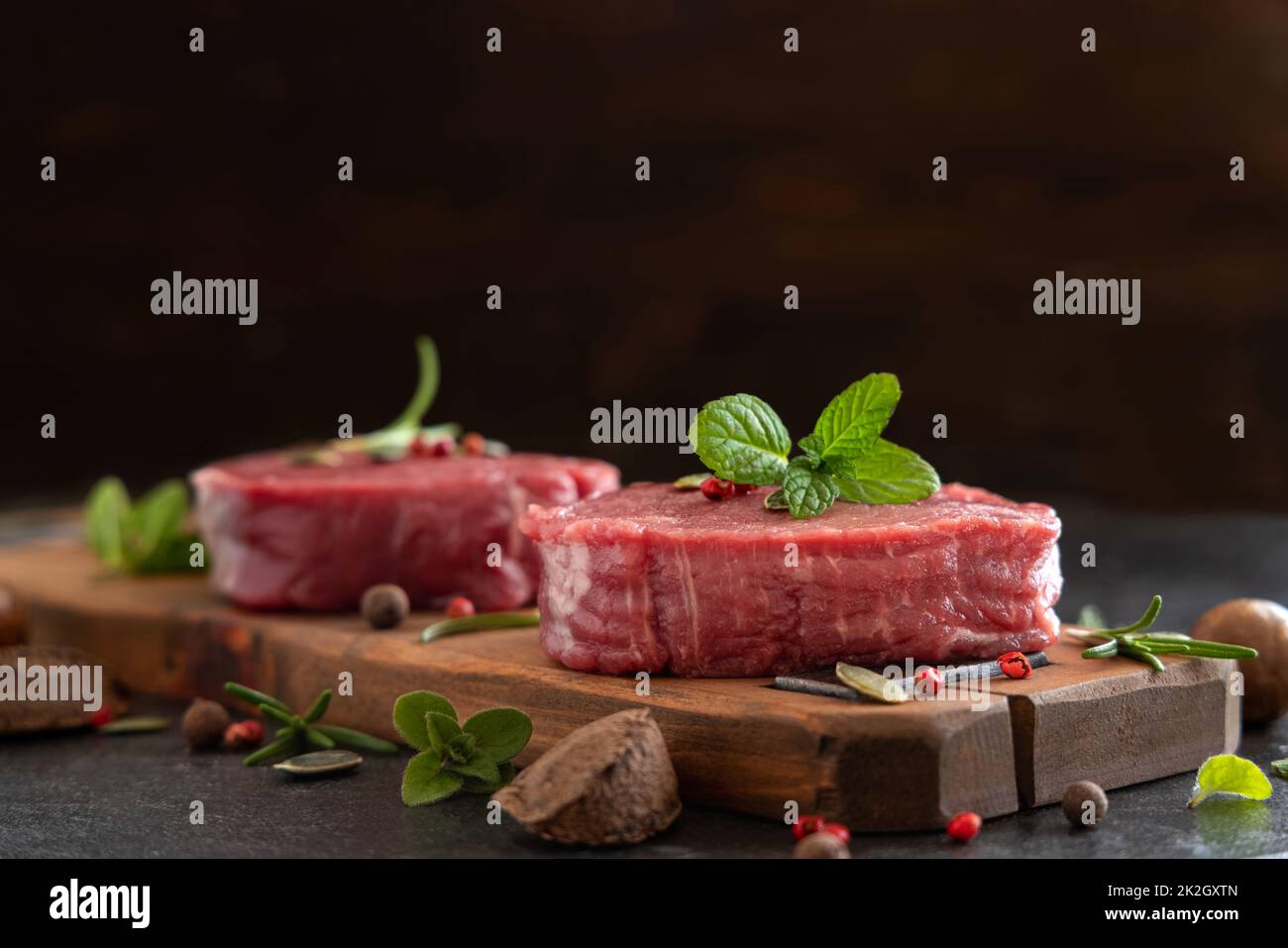 Raw beef fillet steaks with herbs and spices on dark table close up ...
