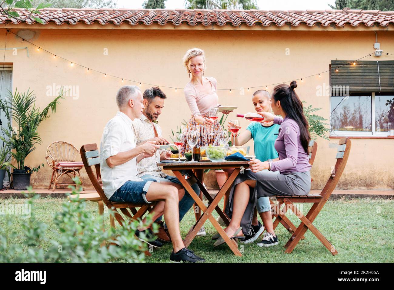 happy woman serving food to his friends enjoying dinner party ...