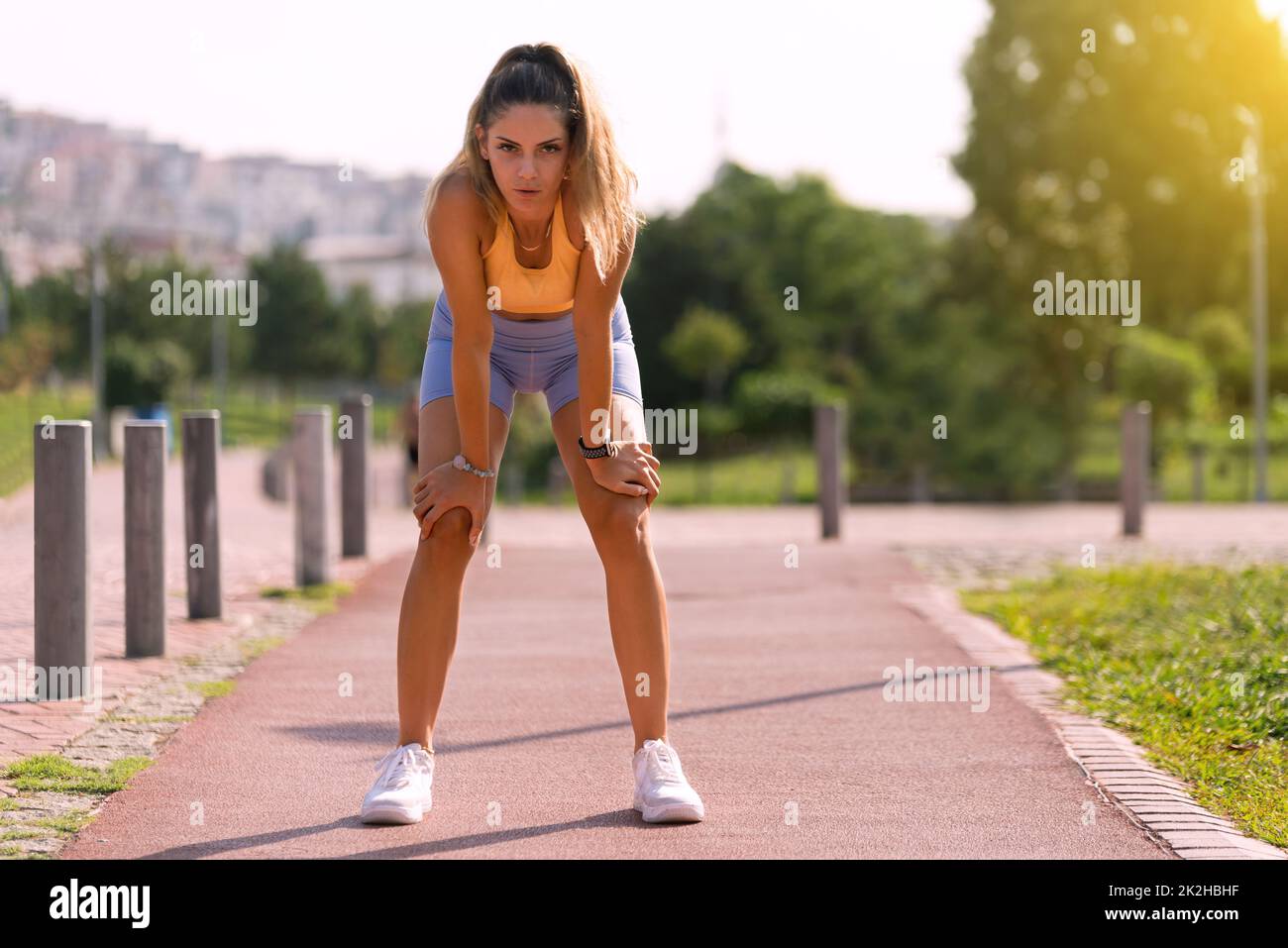 Portrait of a tired woman with holding her knees woman after an exercise or running on a running ...