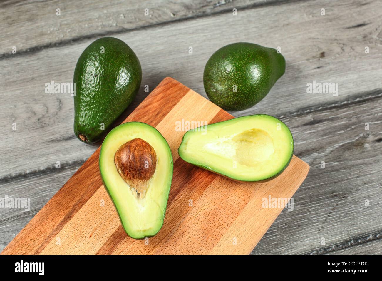Tabletop view, chopping board on gray wood desk, avocado cut in half ...