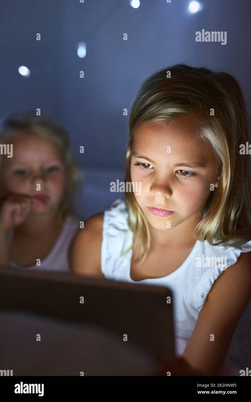 Bedtime in the age of the app. Shot of two little girls using a digital tablet before bedtime ...